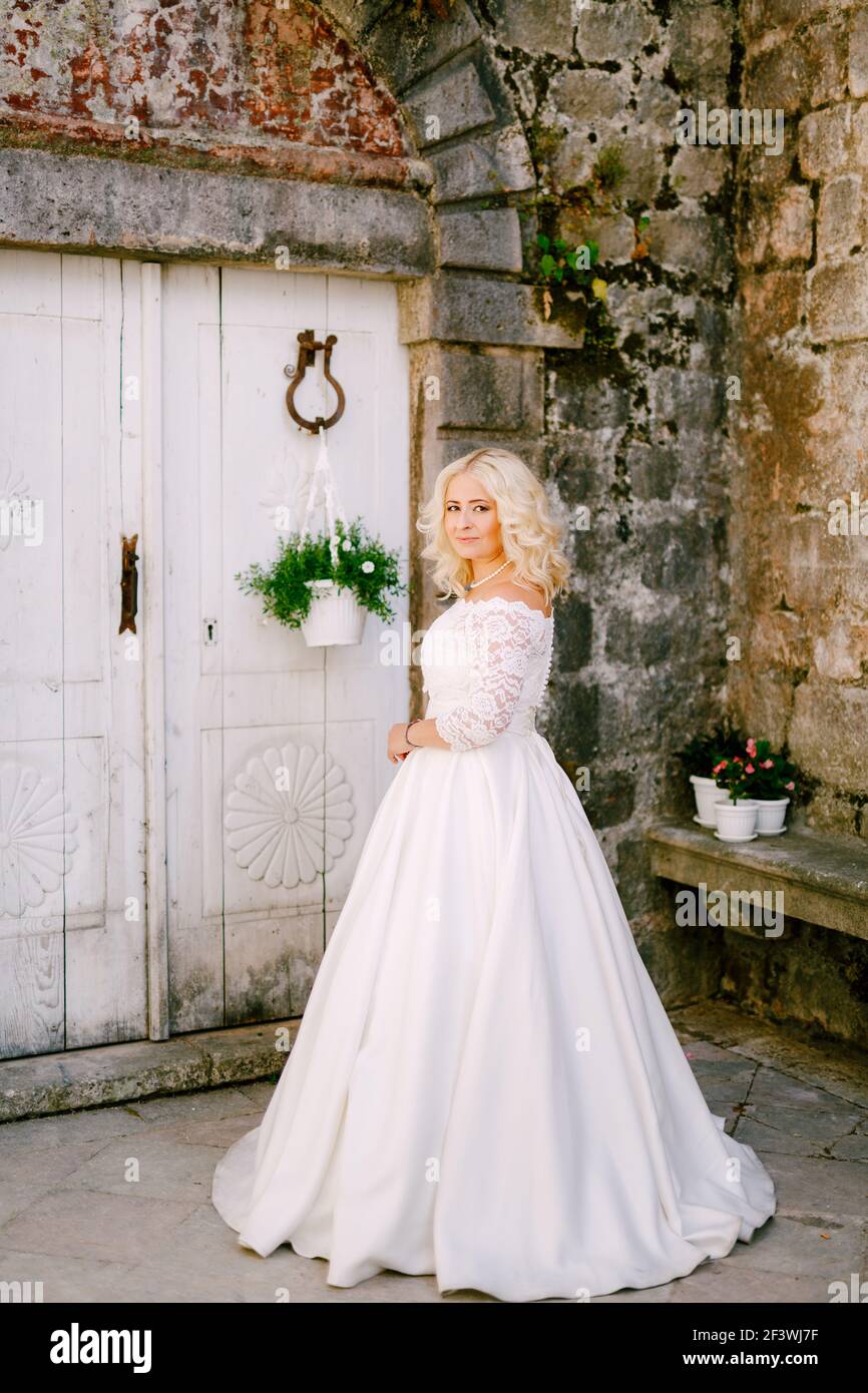 A bride stands in front of an old brick building near a white wooden ...