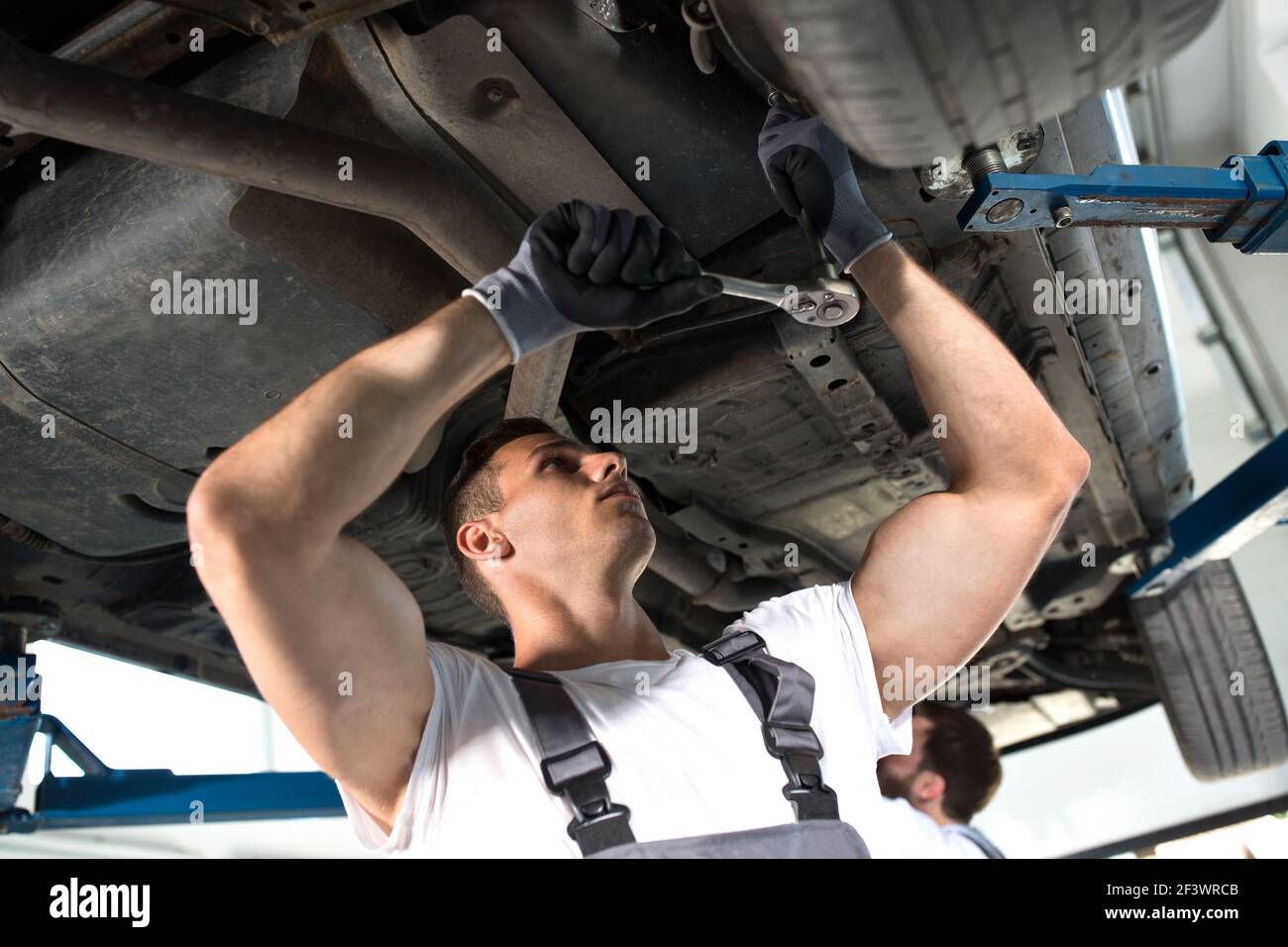 Strong mechanic repairman under the car in a workshop Stock Photo - Alamy