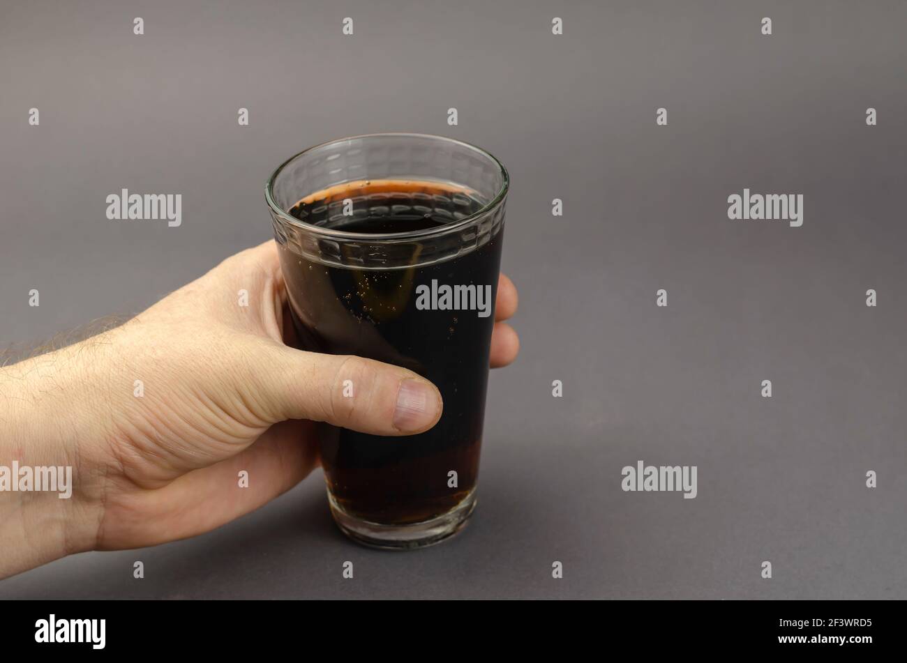 Hand and glass of soda on a gray background. A man's hand holds a full ...