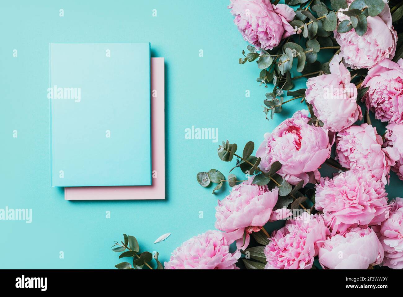 Feminine workspace with notebook, pink peony, eucalyptus flower on blue ...