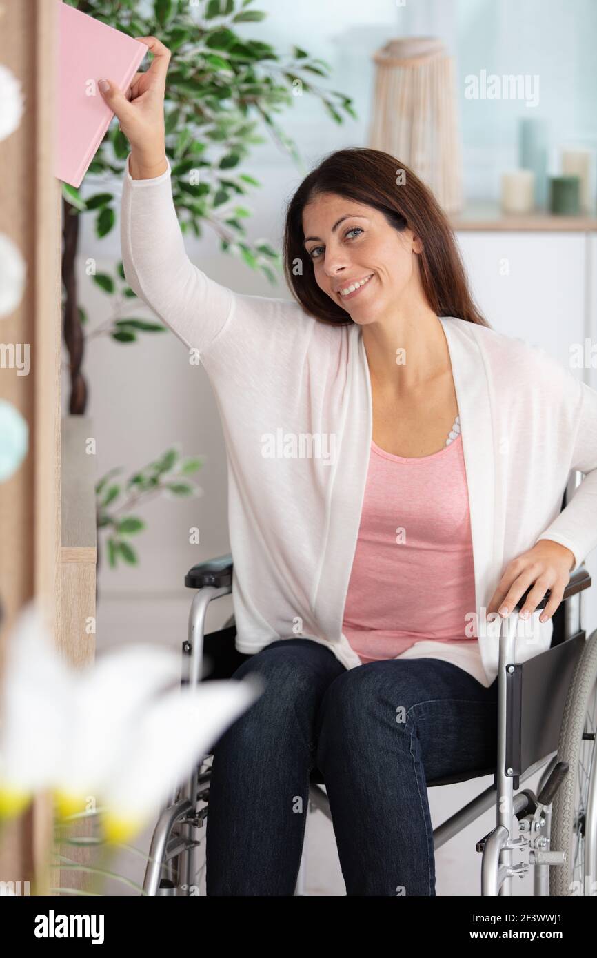 smiling woman sitting in wheelchair reaching for a book Stock Photo - Alamy