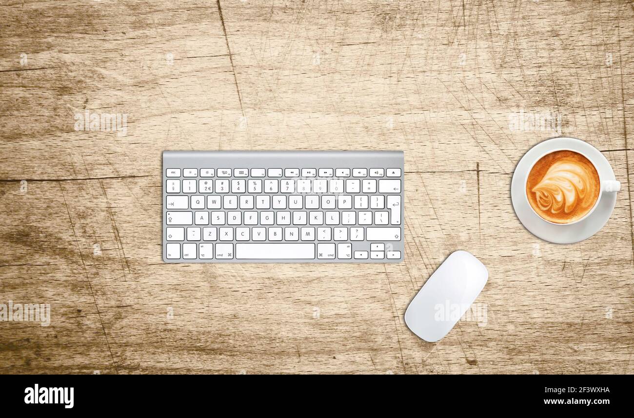 A flat lay of a keyboard, a mouse, and a cup of coffee on wooden ...