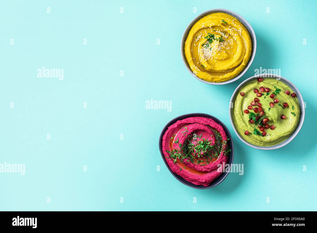 Colorful hummus bowls - green, yellow and beetroot hummus on dark ...