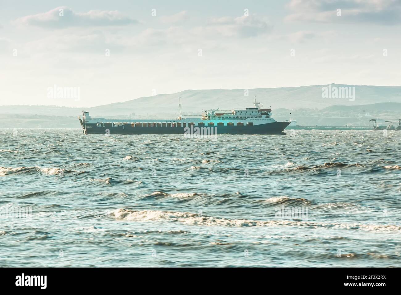 Sea cargo ferry in the stormy sea. Mountanious background Stock Photo ...