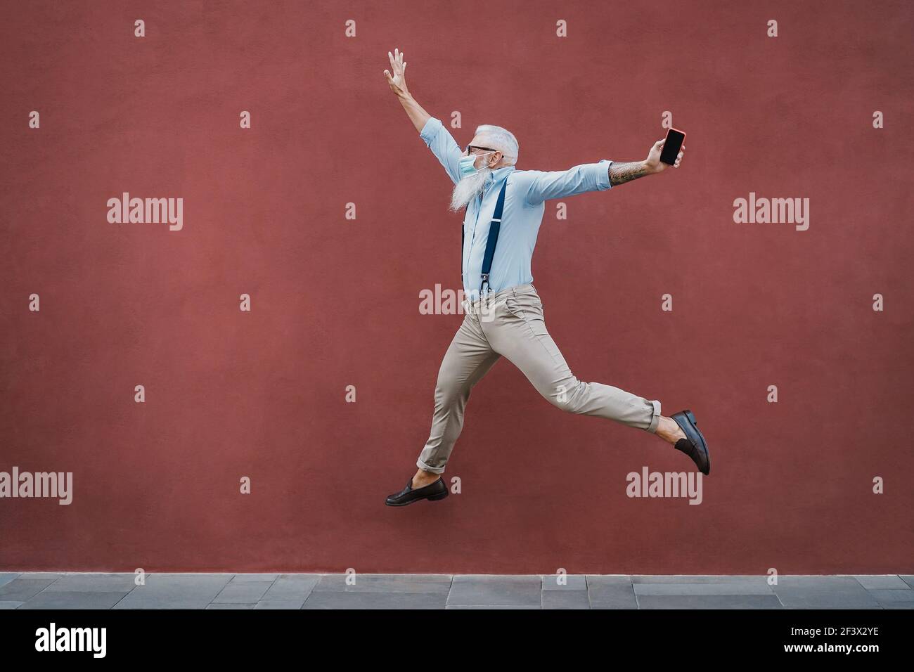 Senior crazy man jumping outdoors while wearing mask with red wall in ...