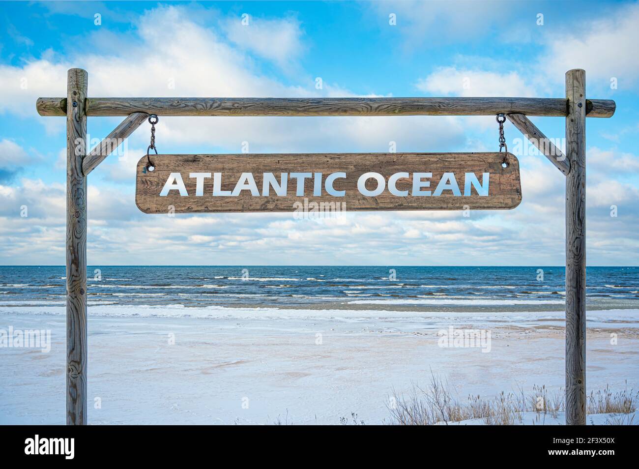 Wooden sign with Atlantic ocean text against sea, blue sky and beach ...