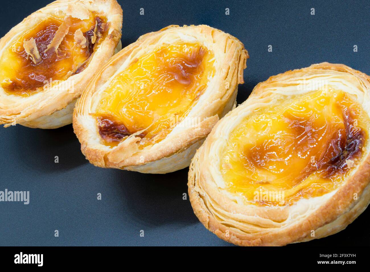 Three small custard tarts on a dark grey background Stock Photo - Alamy