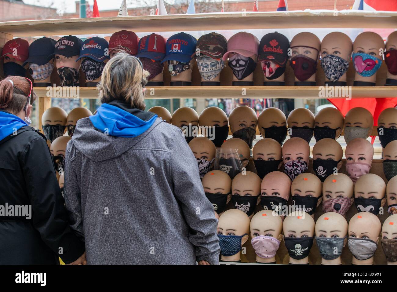 People look at a display of mannequin heads wearing face masks for sale ...