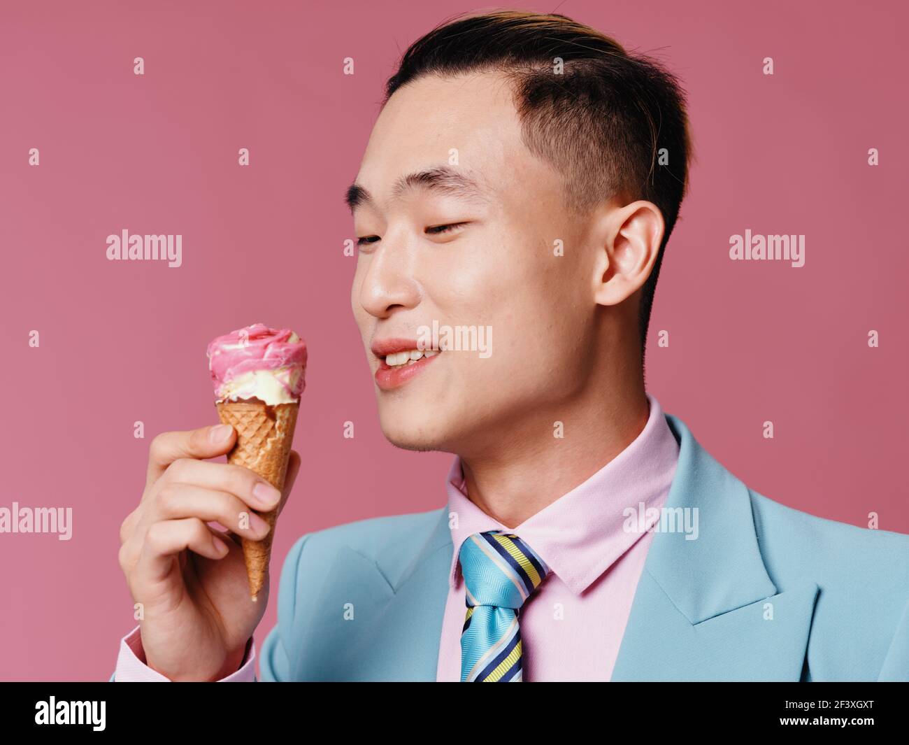 A handsome man in a classic suit examines an ice cream cone on a pink ...