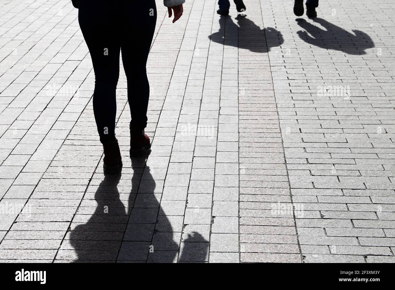 Silhouette and shadow of woman walking on a street towards two men ...