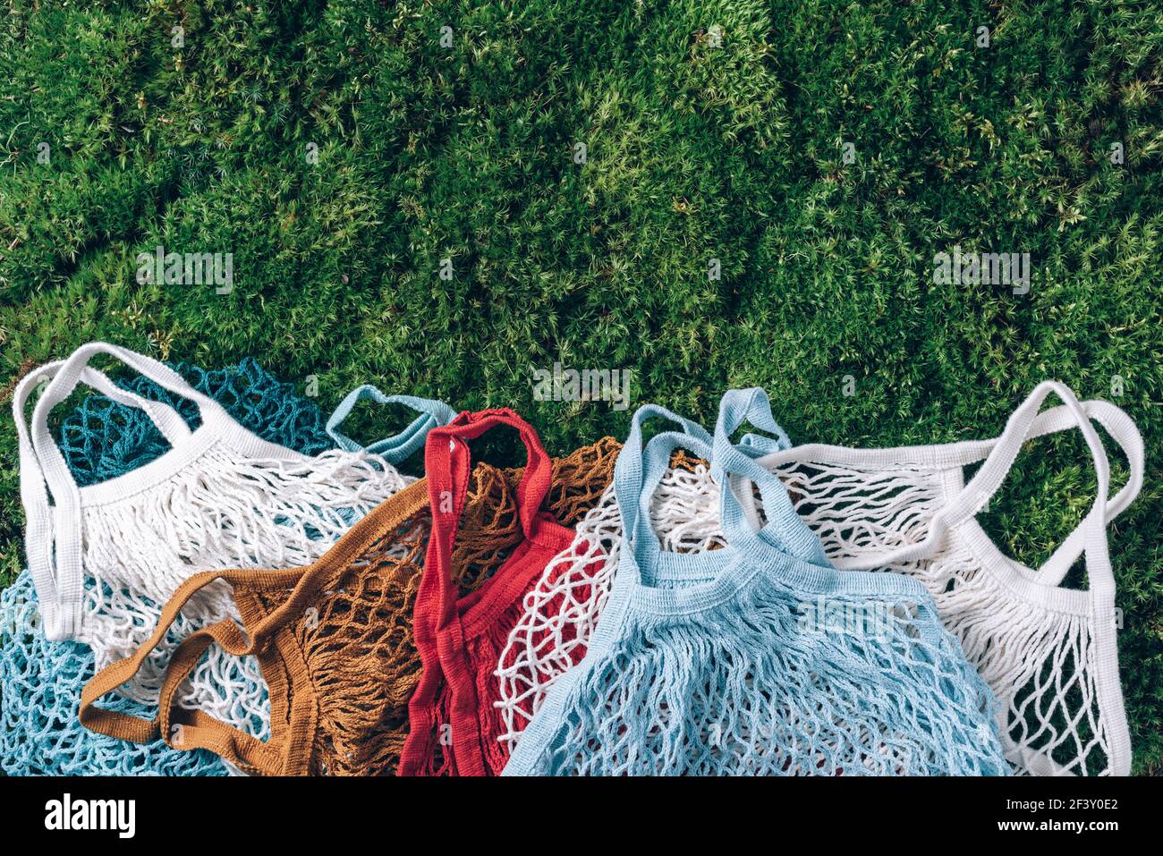 Colorful reusable net bags or mesh shoppers on green grass, moss ...
