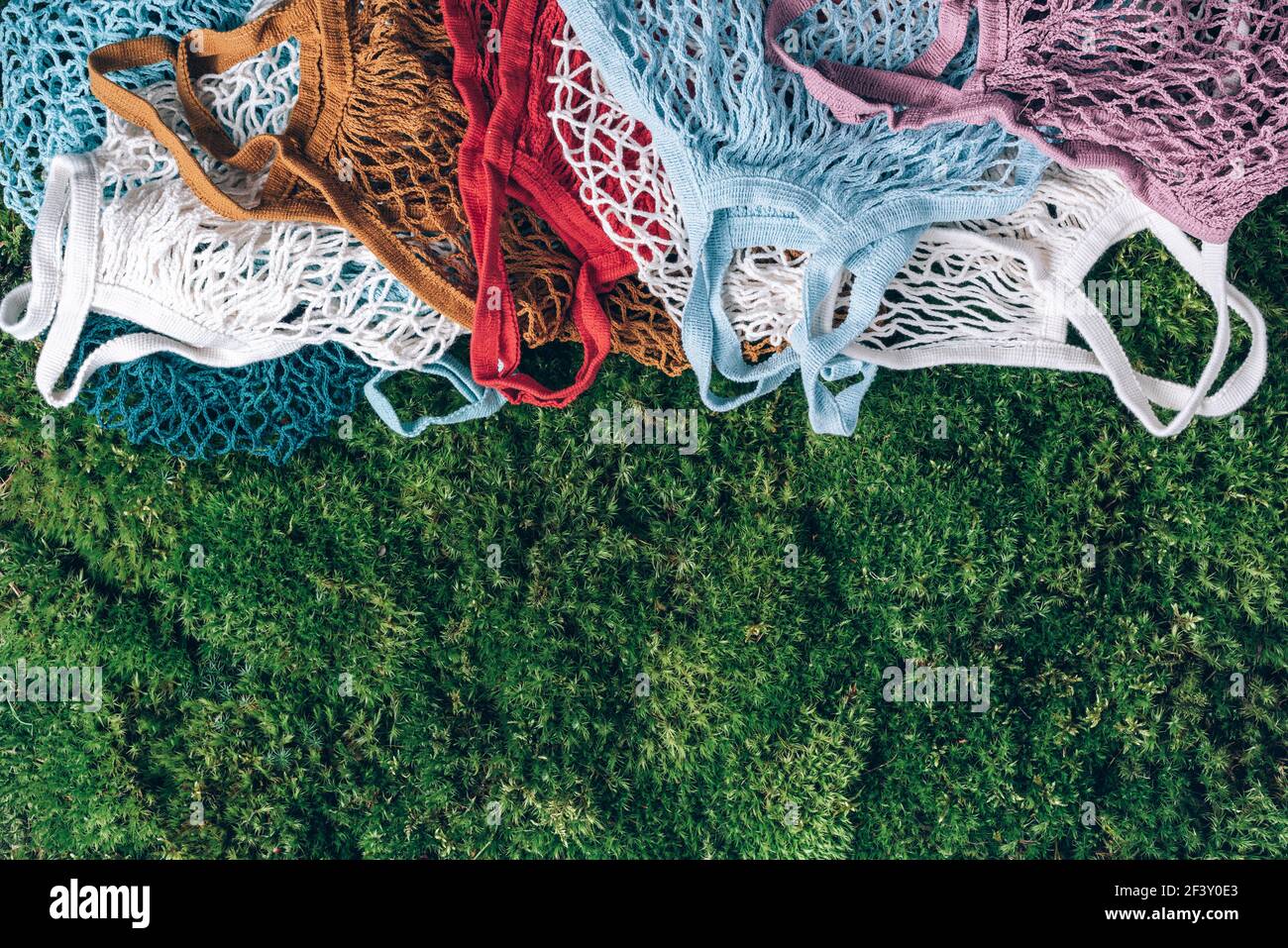 Colorful reusable net bags or mesh shoppers on green grass, moss ...