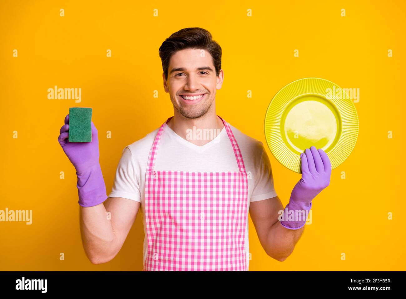 Photo of young handsome happy cheerful smiling man cleaning dishes ...