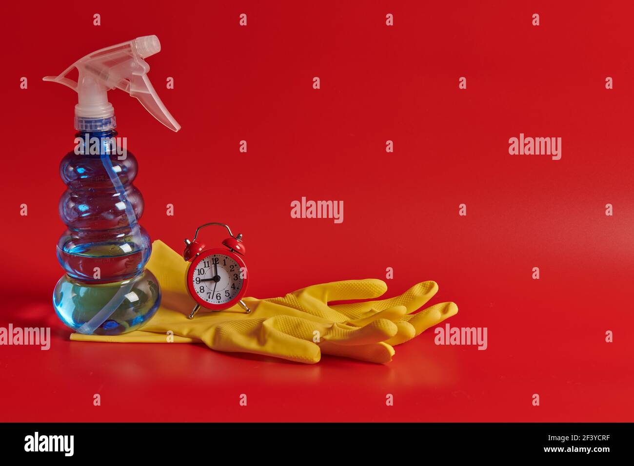 spray bottle and alarm clock and yellow gloves on a red background lie ...