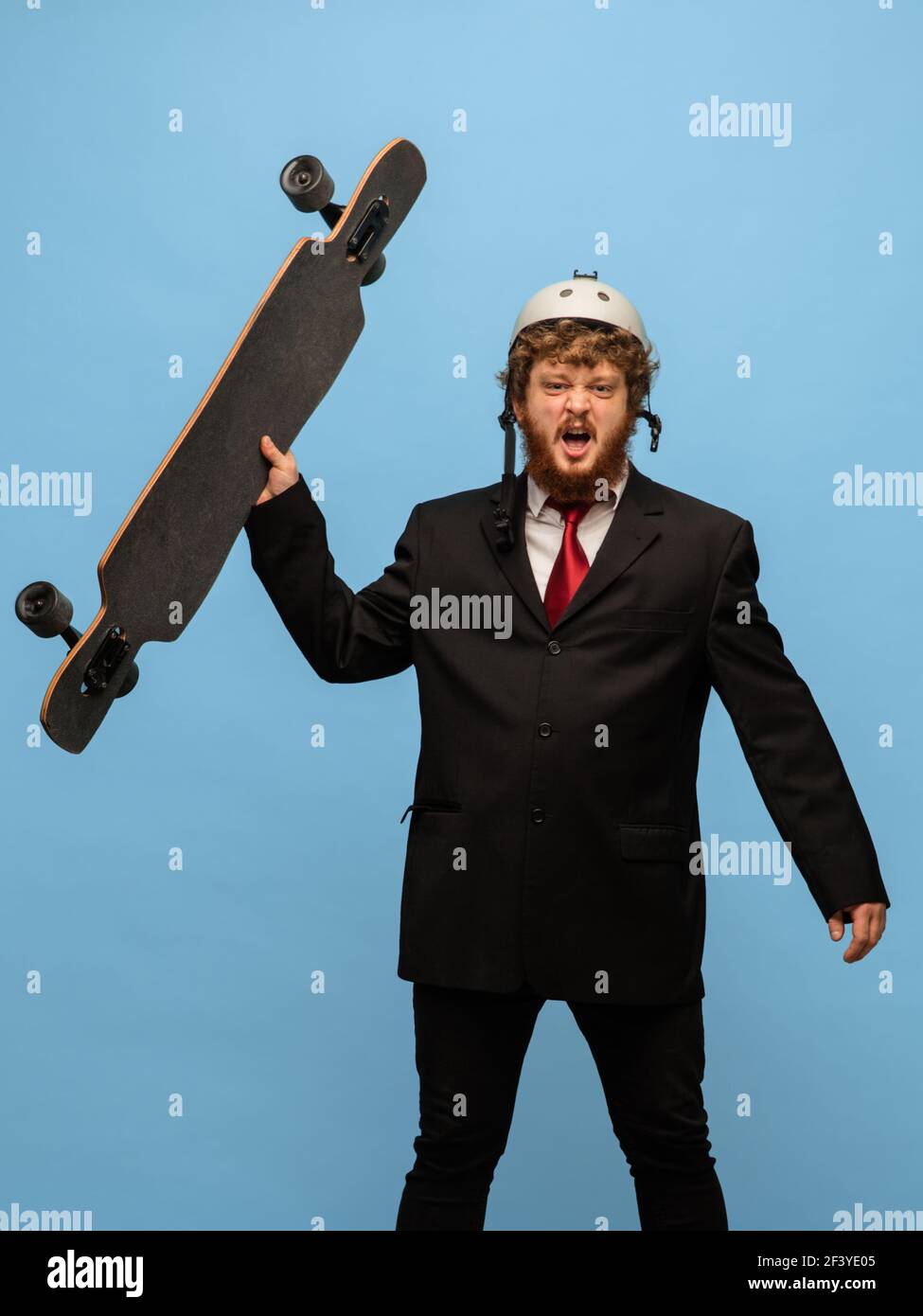 Funny red-headed man in black suit holding longboard isolated on blue ...