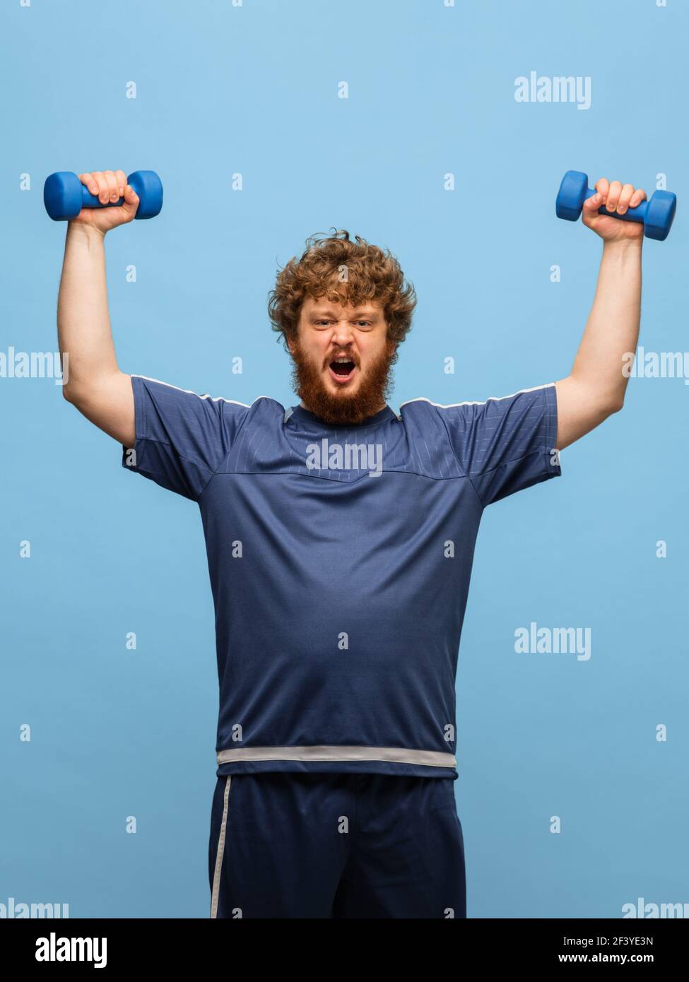 Funny red-headed man in blue sports uniform isolated on blue background ...