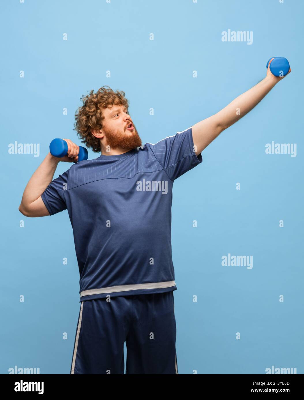 Funny red-headed man in blue sports uniform isolated on blue background ...