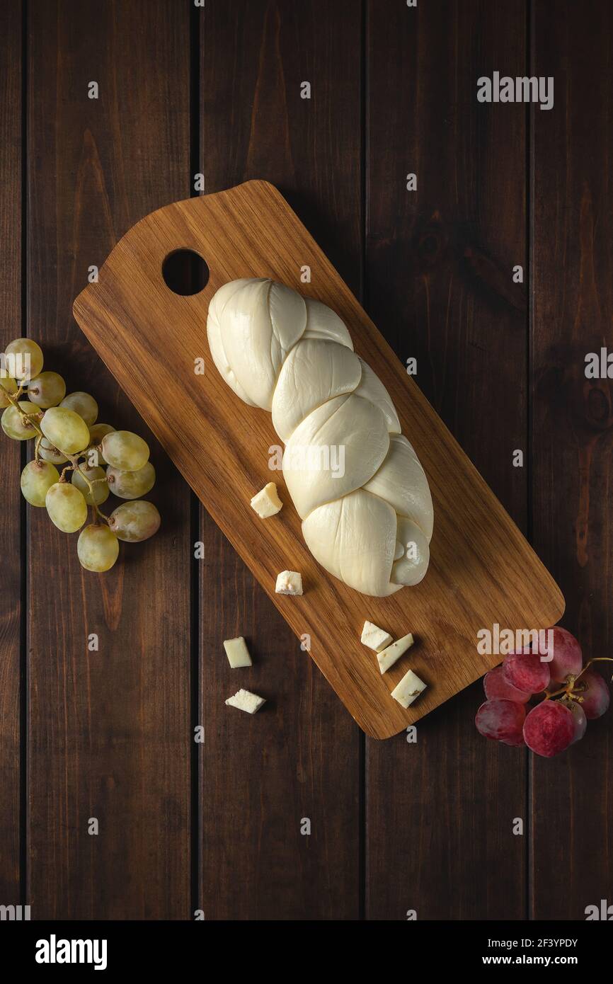 white cheese pigtail with red and green grapes on a wooden cutting ...
