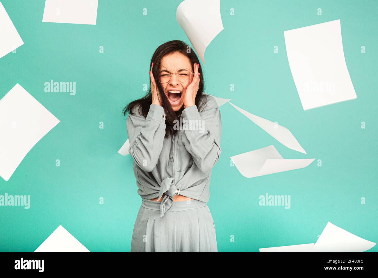 Photo of cute female in glasses is screaming, paper is flying around ...