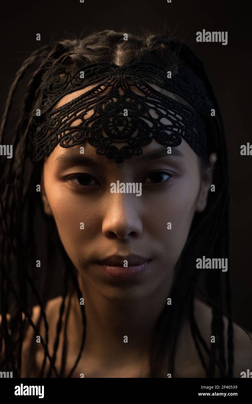 Young asian woman with ethnic braids at studio over dark background ...