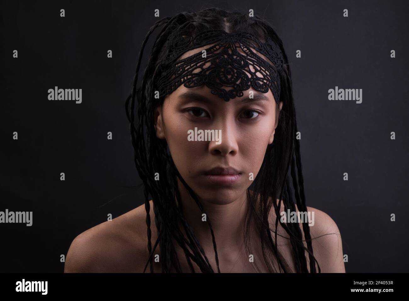 Young asian woman with ethnic braids at studio over dark background ...
