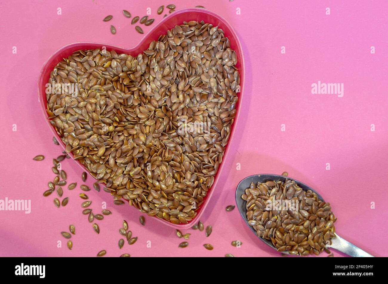 Flax seeds in the shape of a heart on a pink background, top view. Super food. Healthy vegan ...