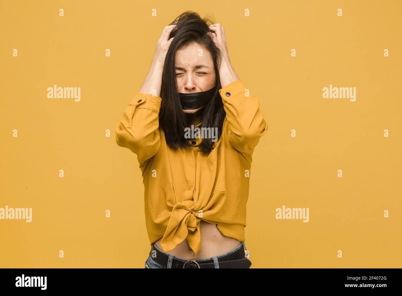 Concept photo of female victim with her mouth taped up, holds her head ...
