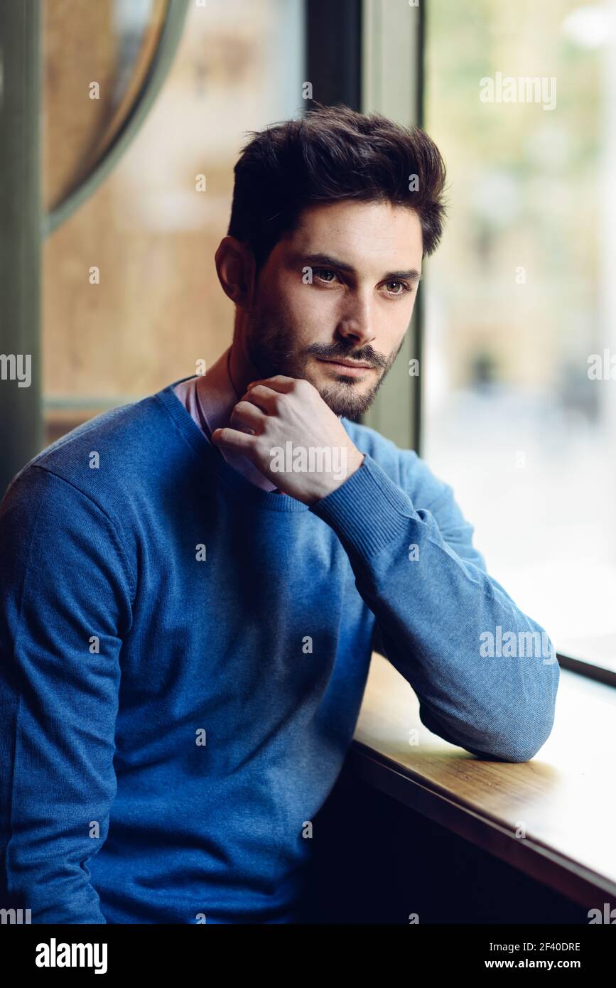 Thoughtful man with blue sweater with lost look near a window in a ...