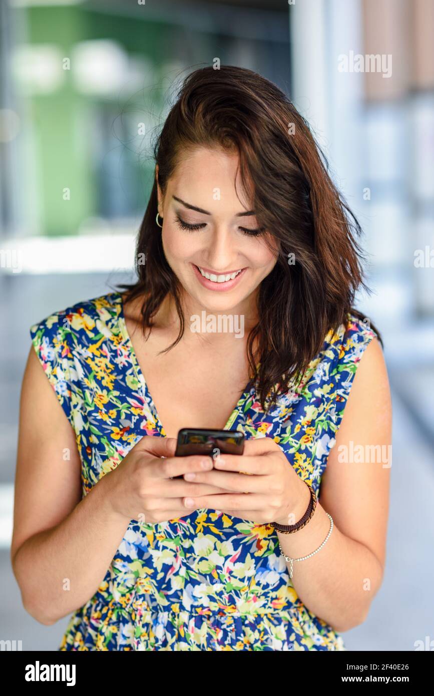 Smiling young woman typing in smart phone outdoors. Girl wearing flower ...