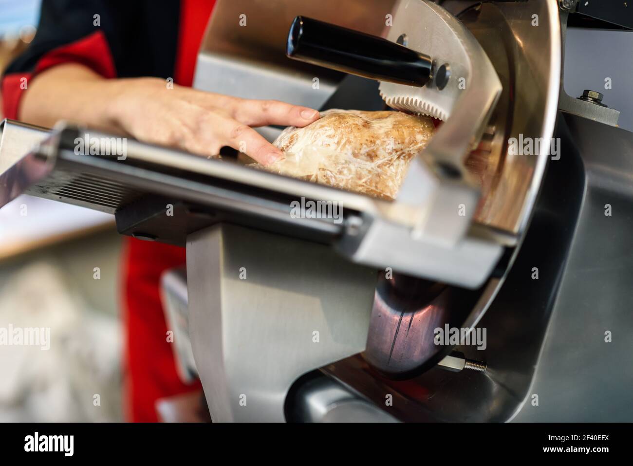 Close-up of female butcher cutting york ham in a cutting machine inside ...