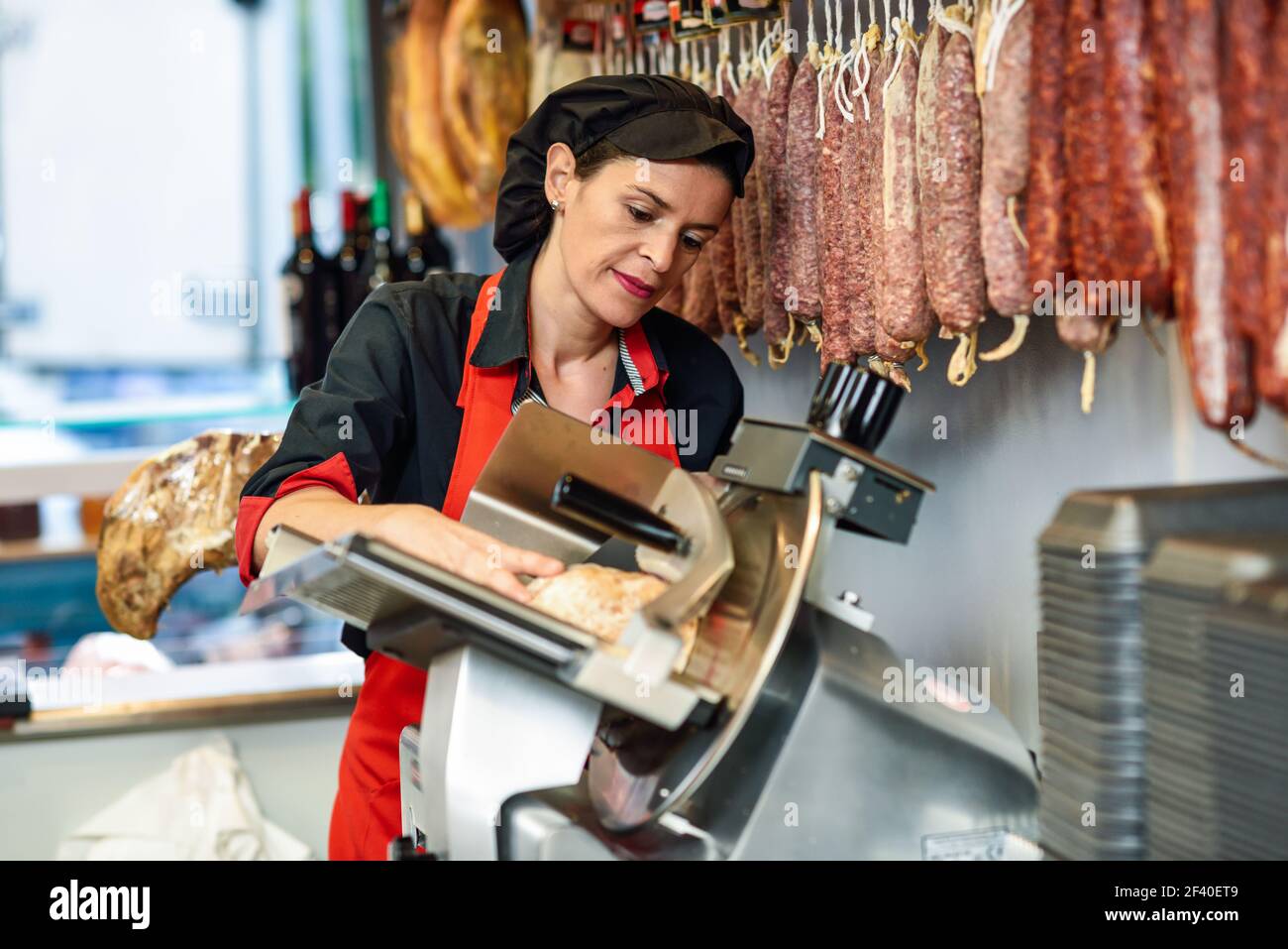 Female butcher cutting york ham in a cutting machine inside a butcher ...
