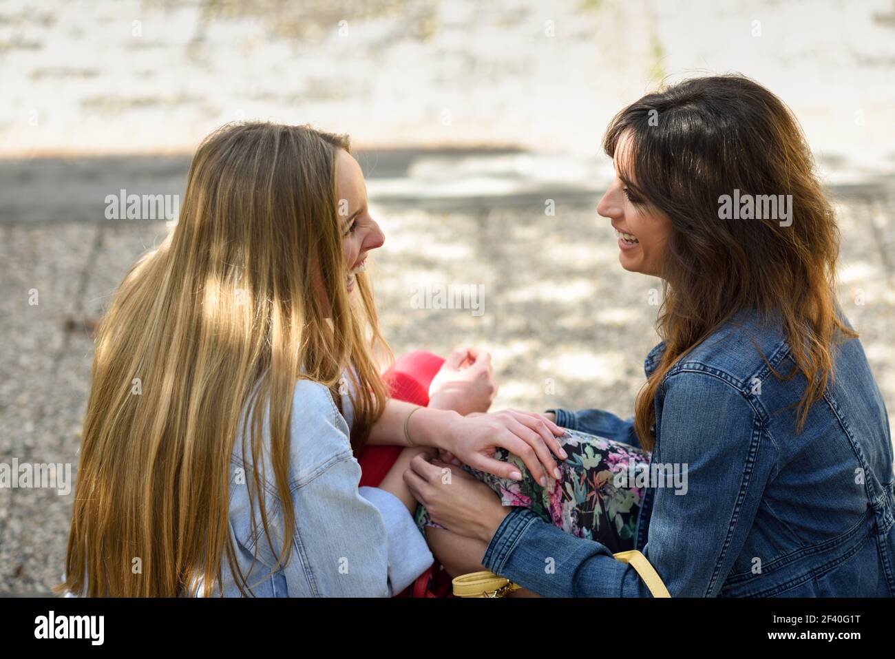 Two young women talking and laughing on urban steps. Two girls wearing ...
