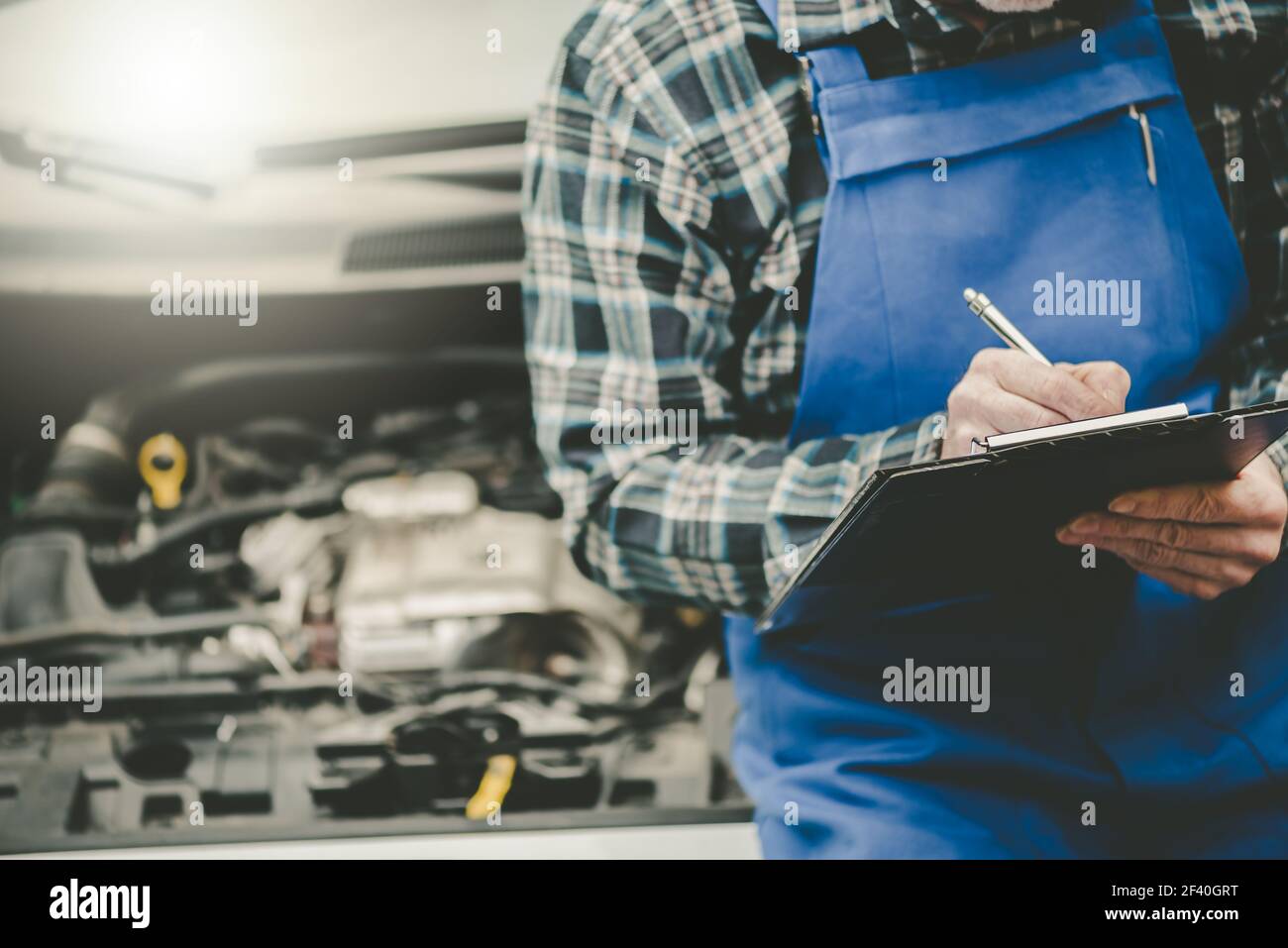 Car mechanic checking a car engine and writing on clipboard Stock Photo ...