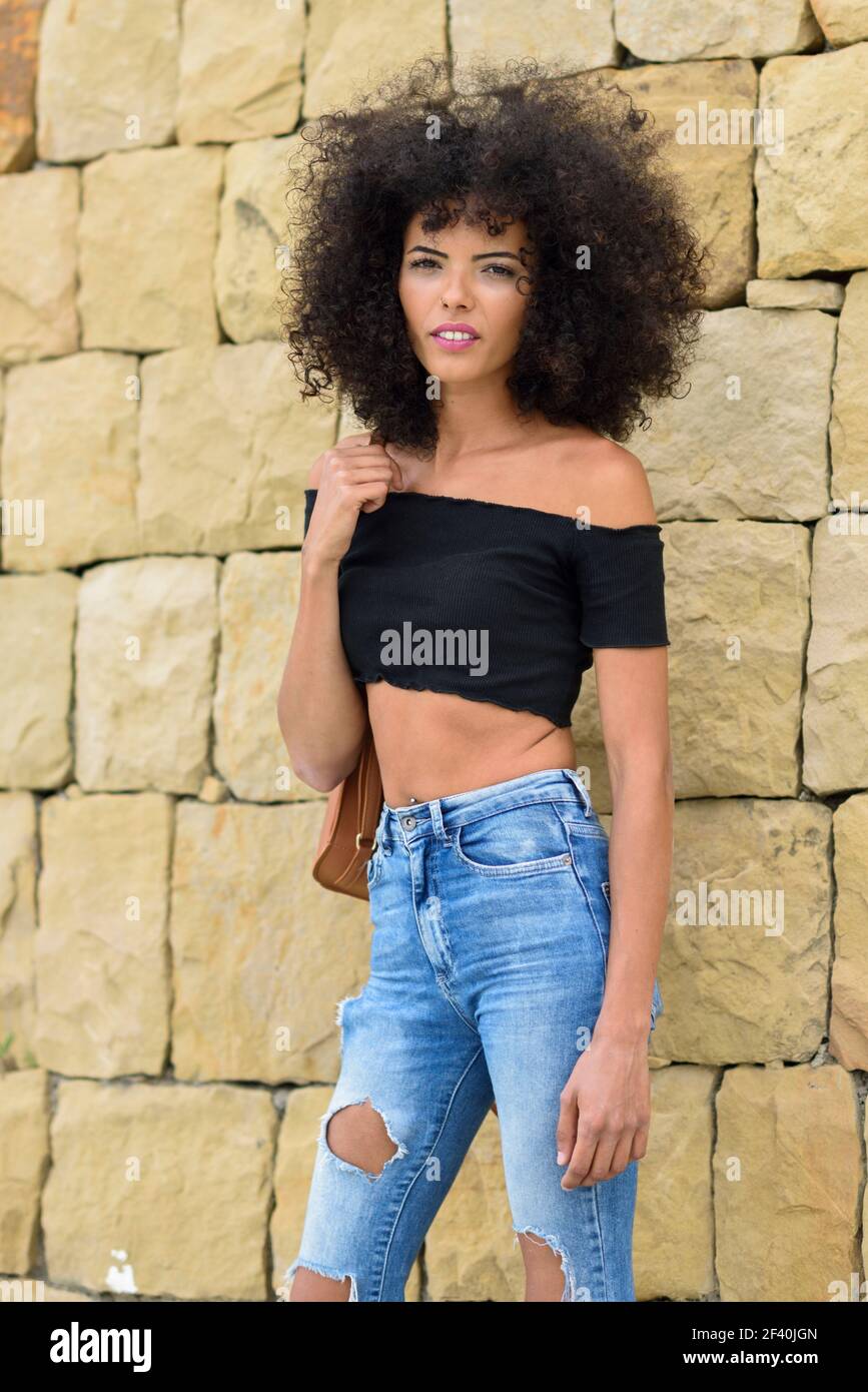 Young mixed woman with afro hair standing on the street. Female wearing ...