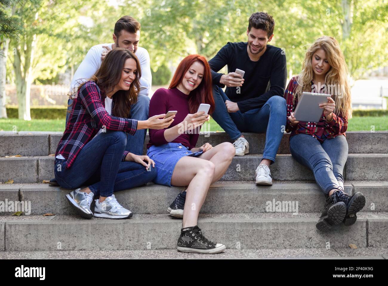 Group of young people using smartphone and tablet computers outdoors in ...