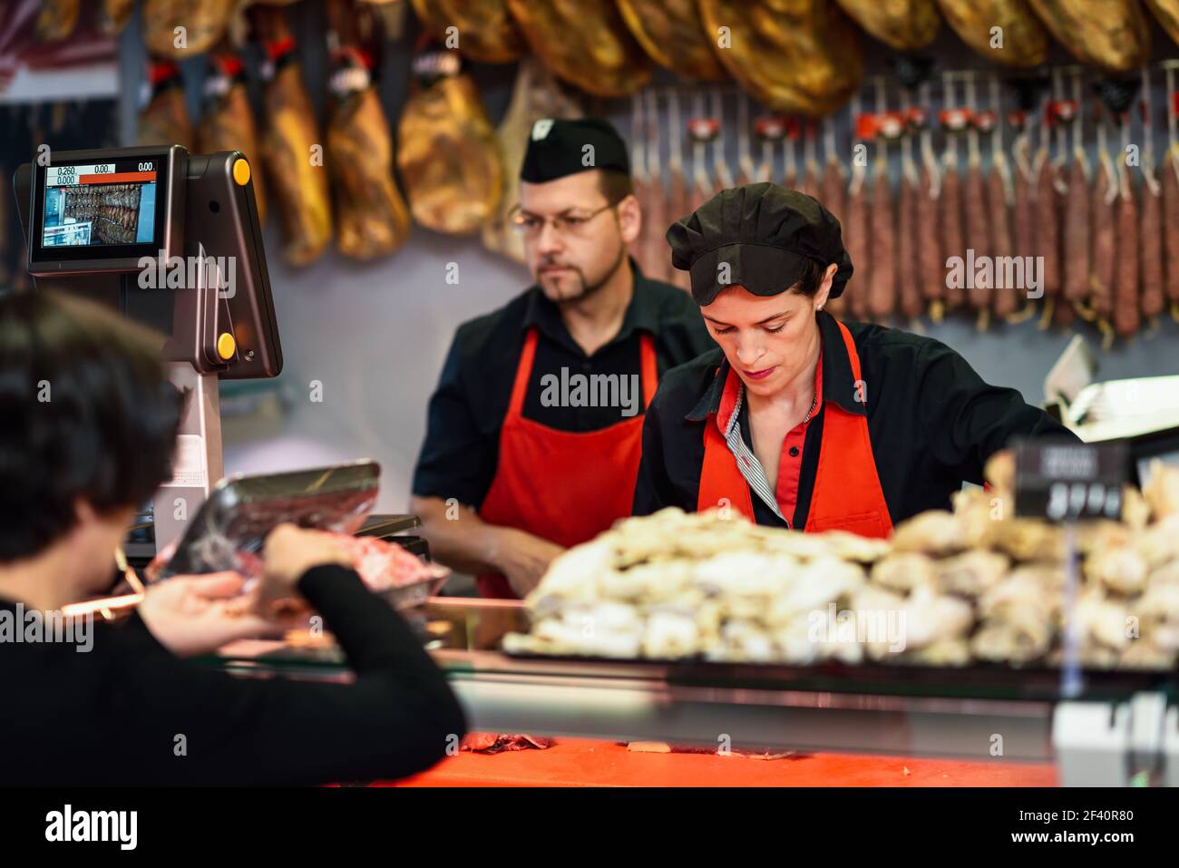 Butchers attending a customer in a butcher’s shop weighing the meat and ...