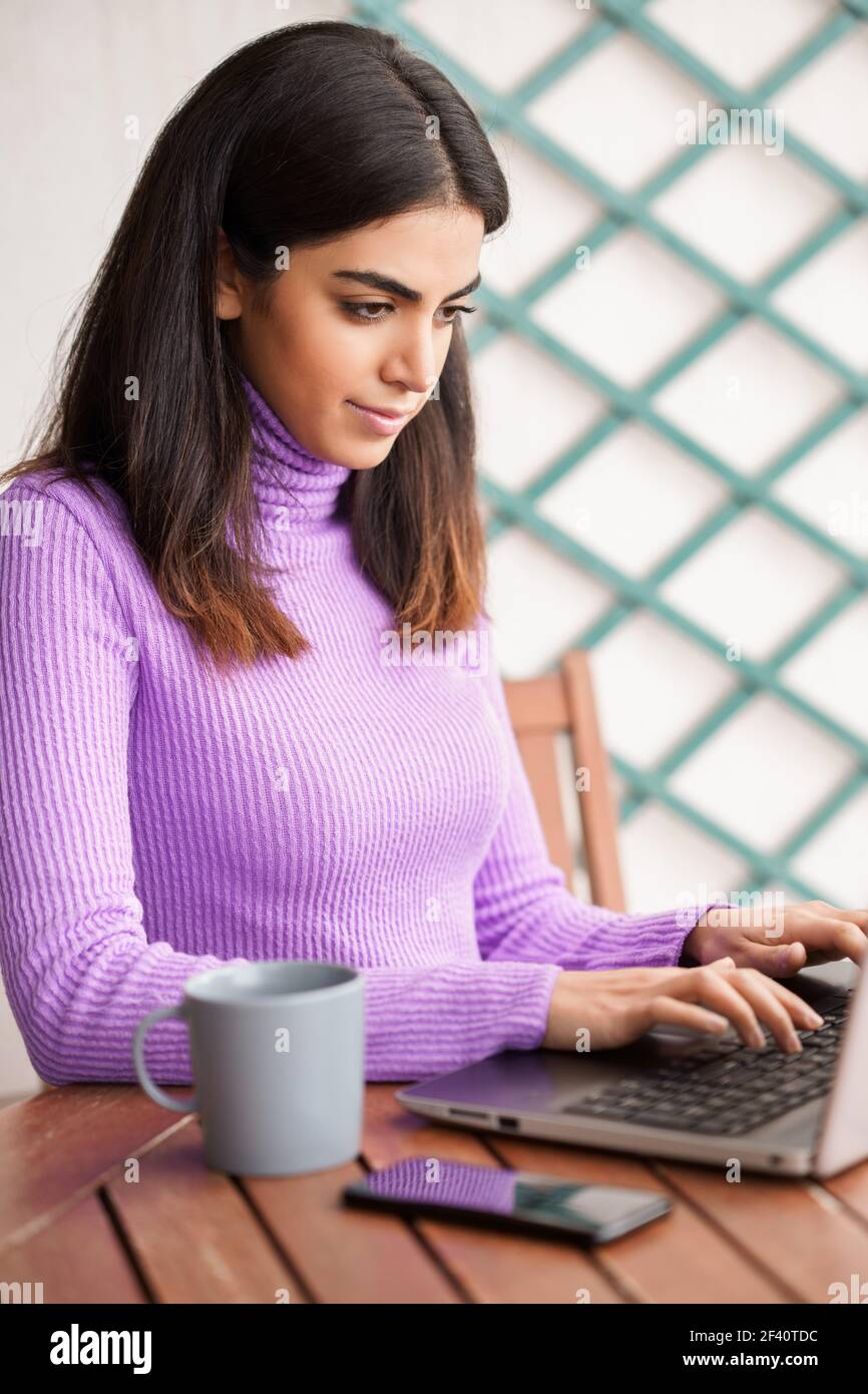Persian woman sitting in an armchair on her balcony using laptop ...