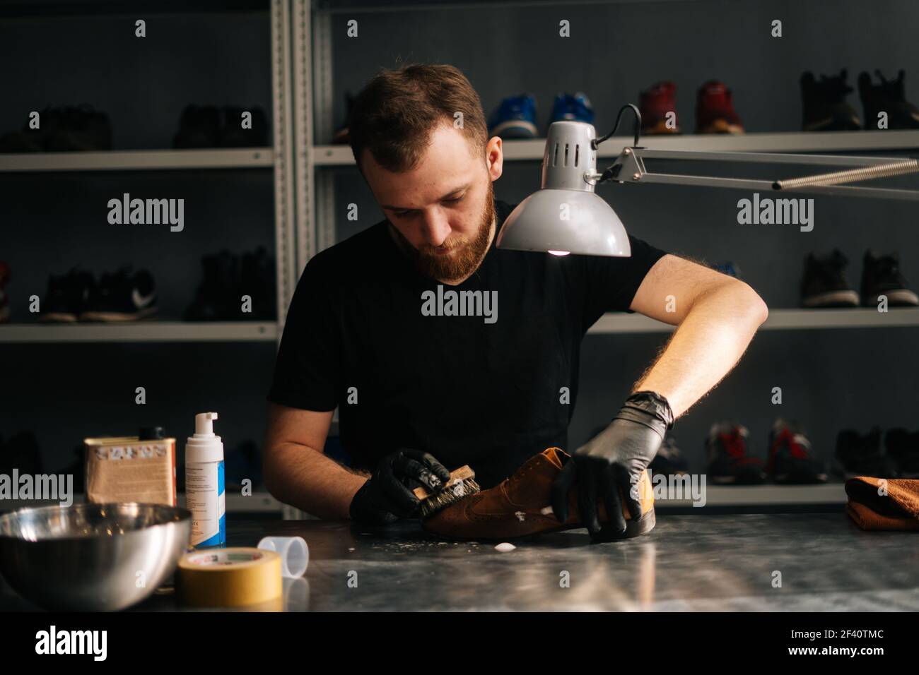 Portrait of shoemaker applying cleaning foam on old worn light brown ...