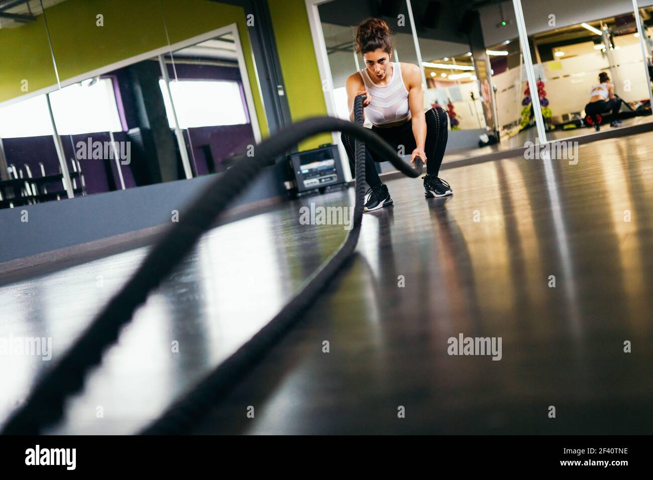 Young and athletic woman using training ropes in a gym. Fitness concept ...