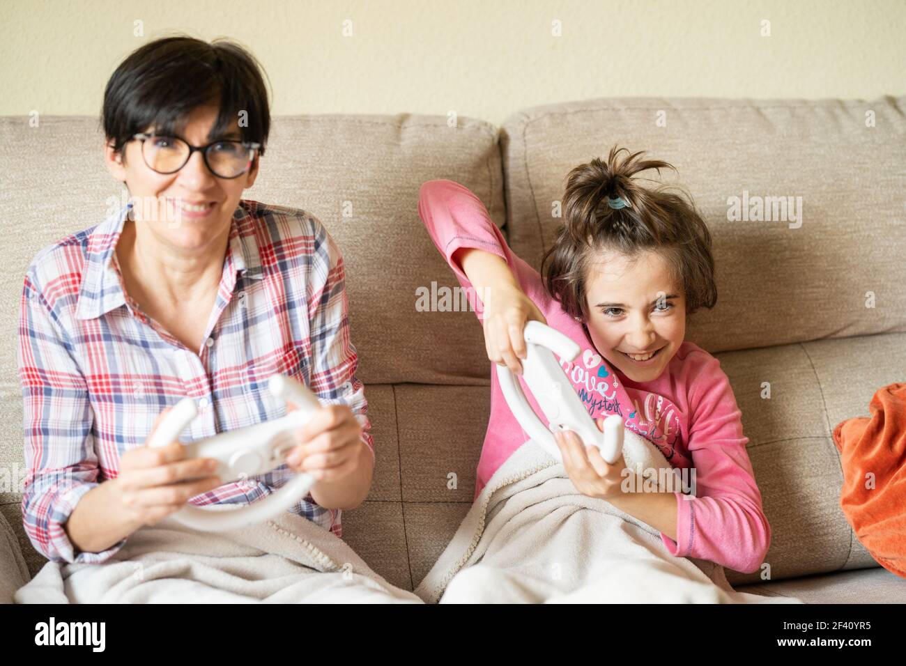 Mother and daughter playing video games at home with a wireless console ...