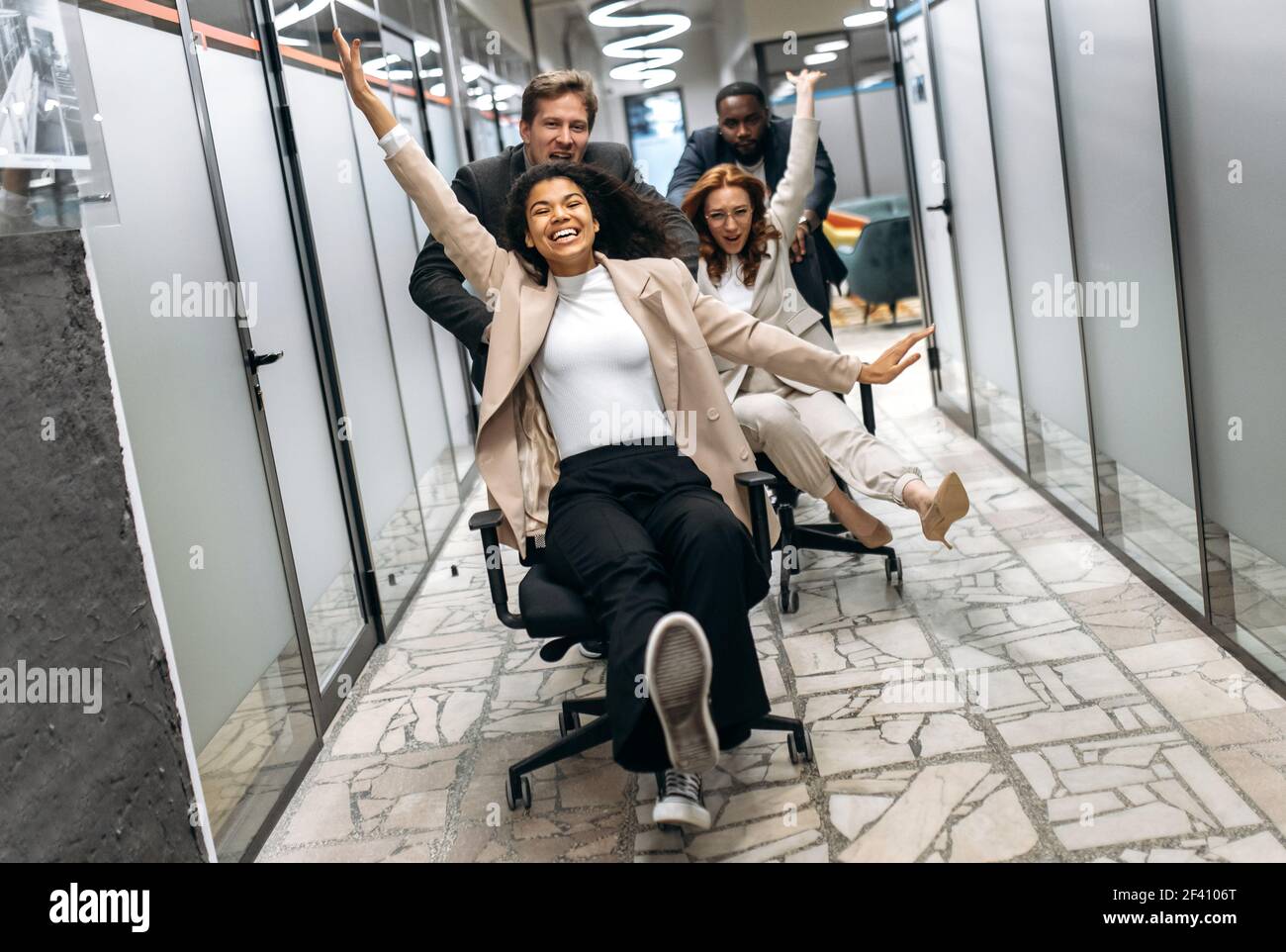 Happy friendly coworkers in formal wear making race on chairs on ...