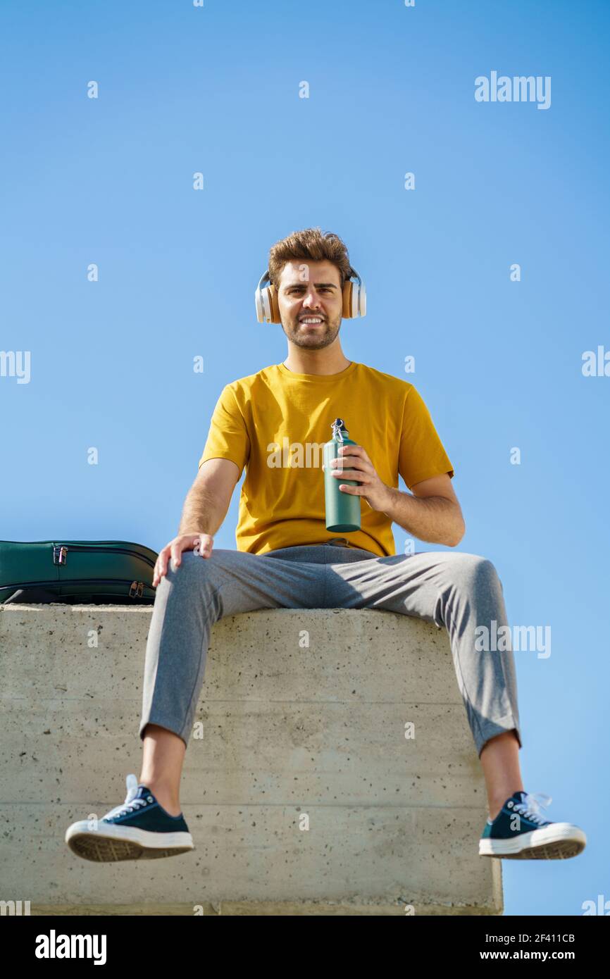 Male student sitting outside using an aluminum water bottle, headphones ... Male student sitting outside using an aluminum water bottle, headphones ...