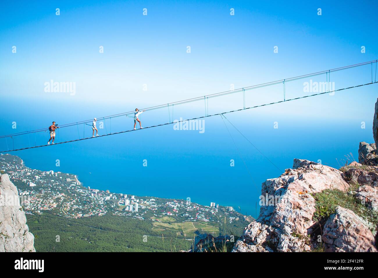 Family crossing the chasm on the rope bridge. Black sea background ...