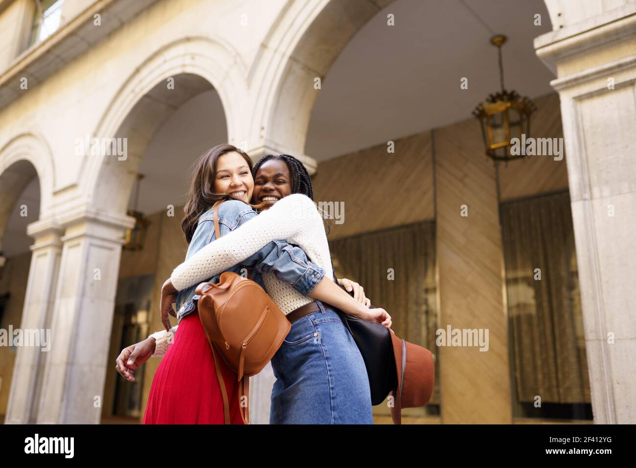 Two friends happy to see each other on the street hugging. Multiethnic ...