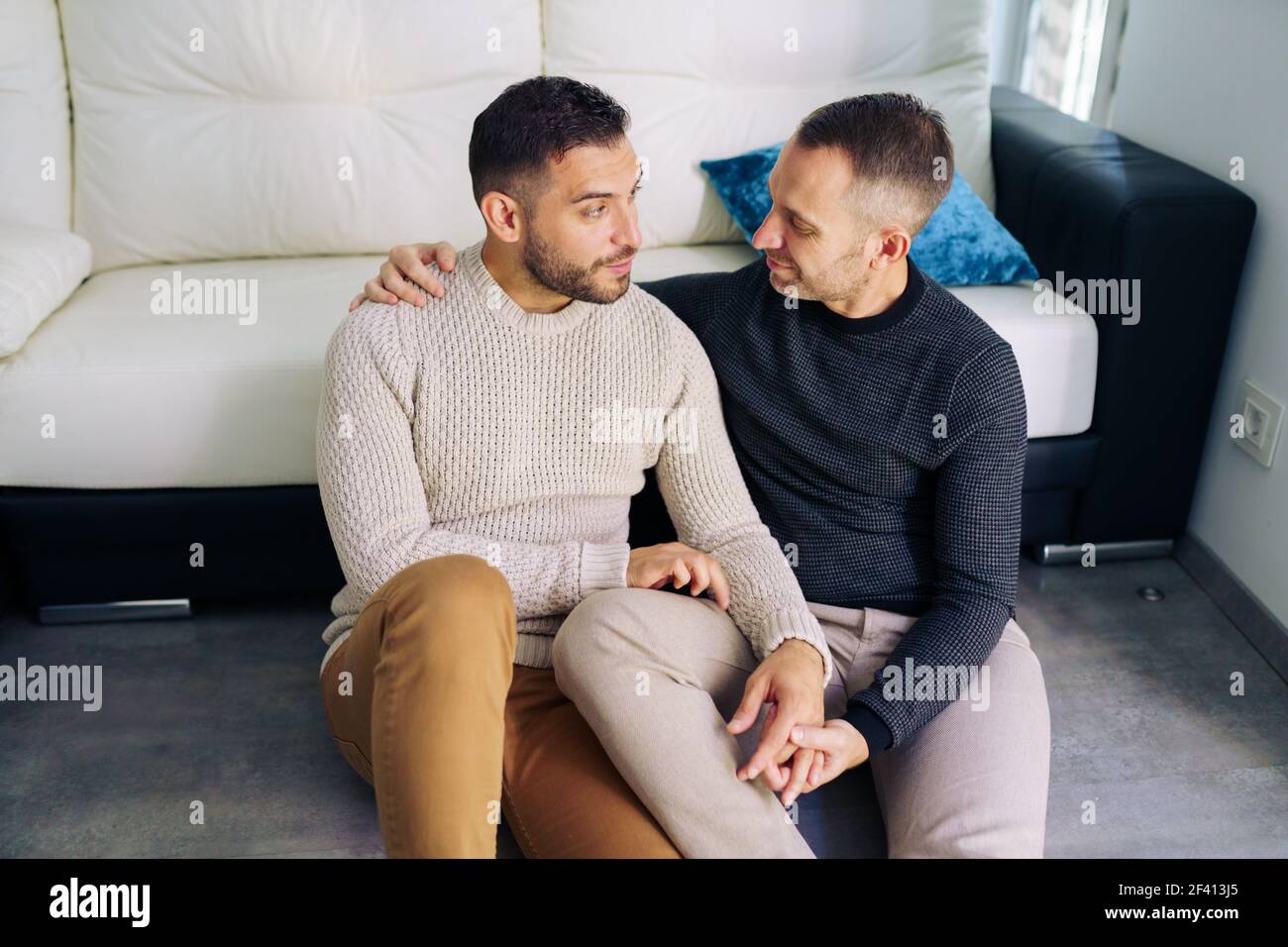Gay couple sitting near the couch at home in a romantic moment ...