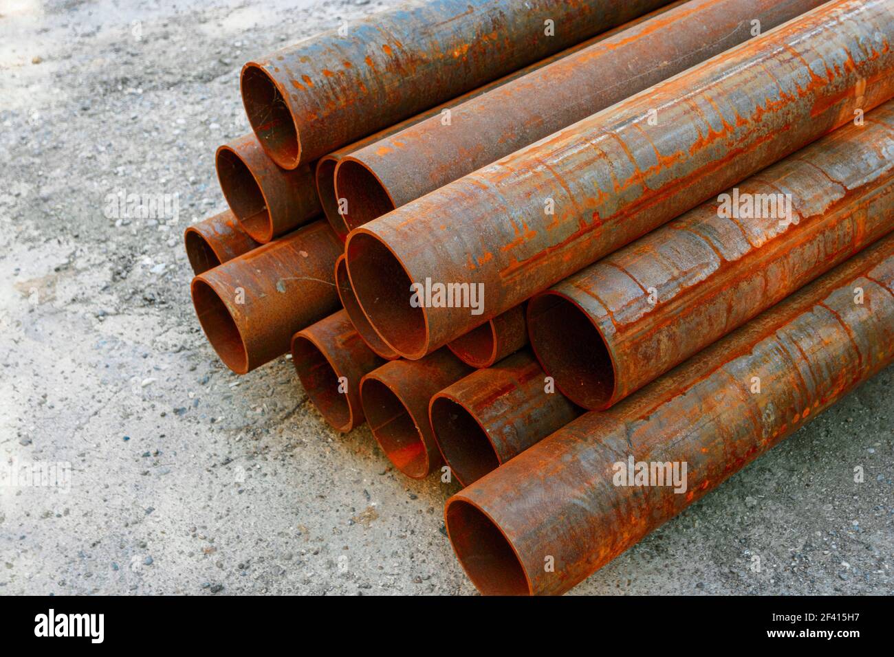 Iron pipes covered with rust in stack on ground in warehouse. Iron ...