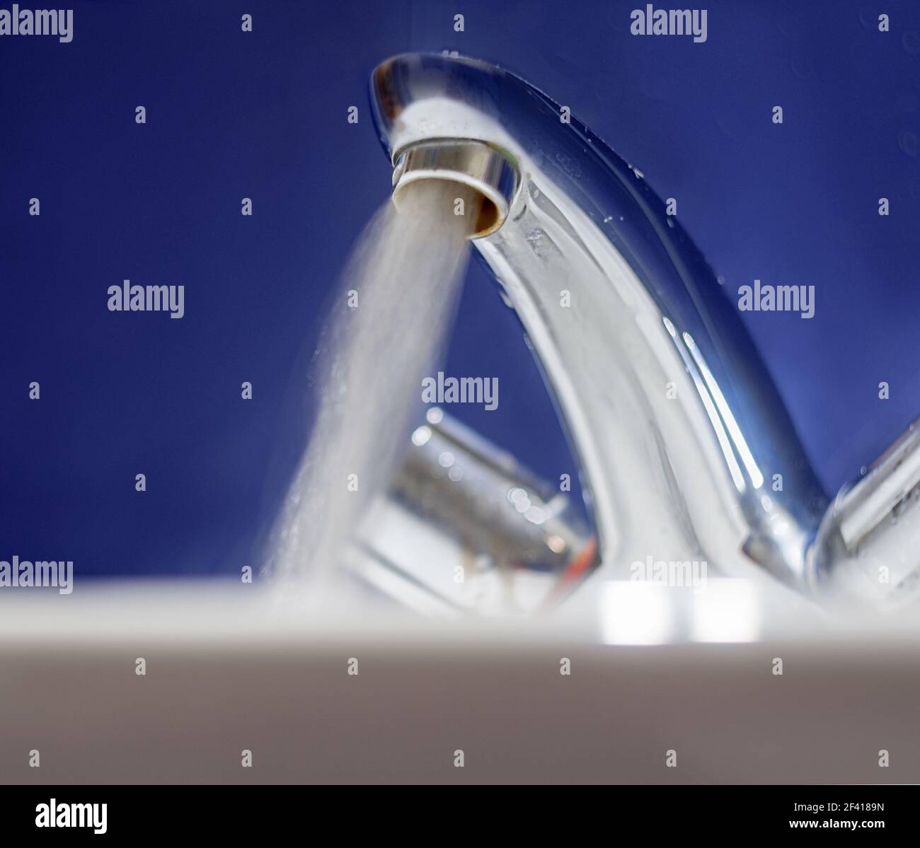 Chrome water tap with water flow from below view on blue background ...