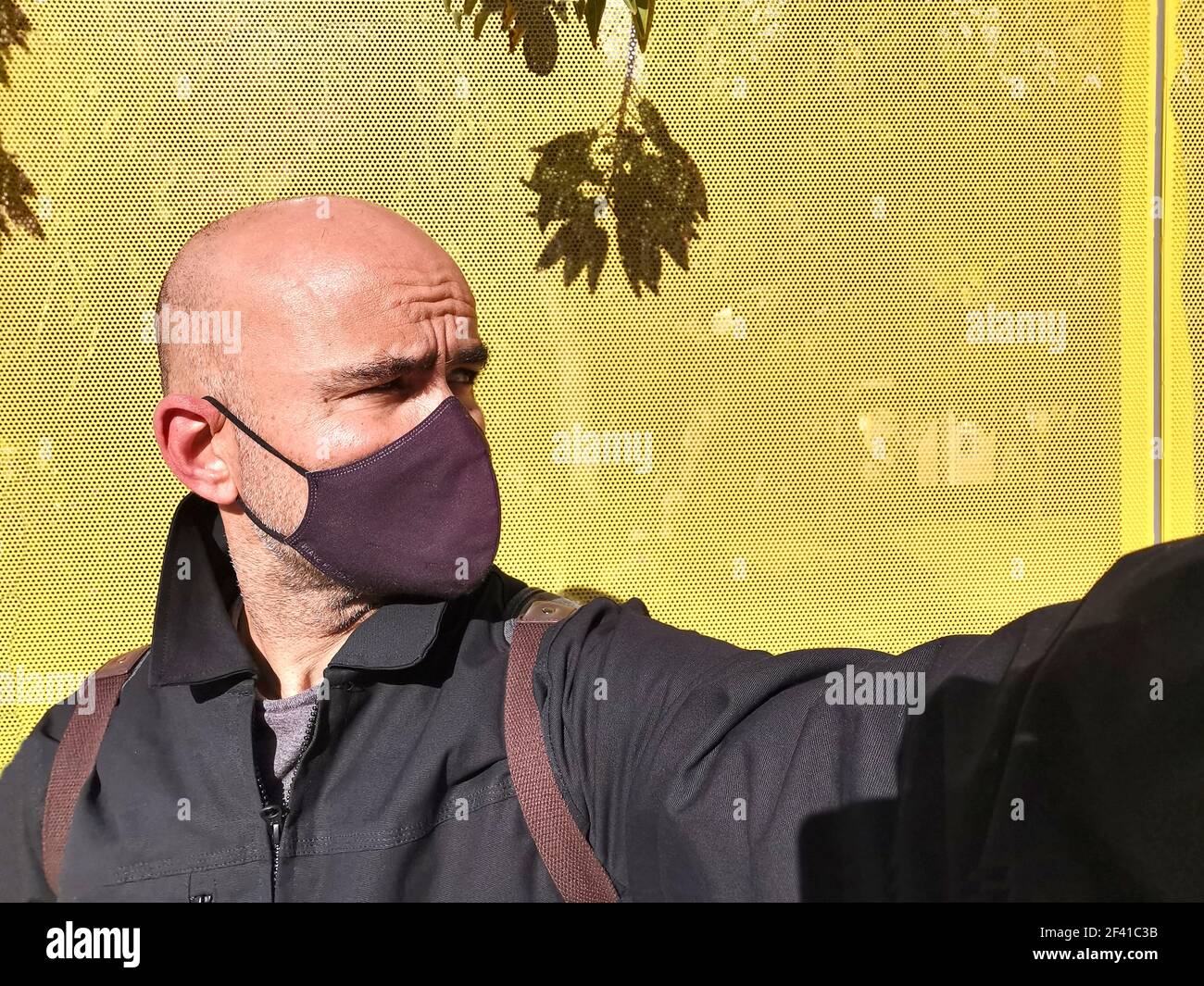 A bald handsome Spanish man with a mask doing a selfie on a yellow ...