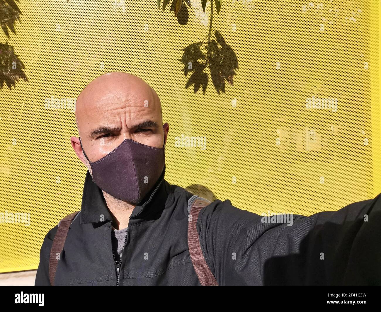 A bald handsome Spanish man with a mask in the street on a yellow ...