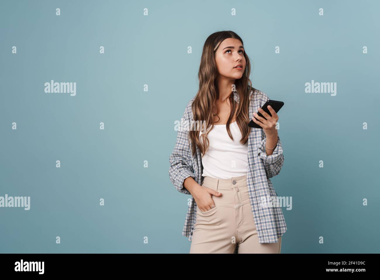 Thinking beautiful girl looking upward while using mobile phone ...